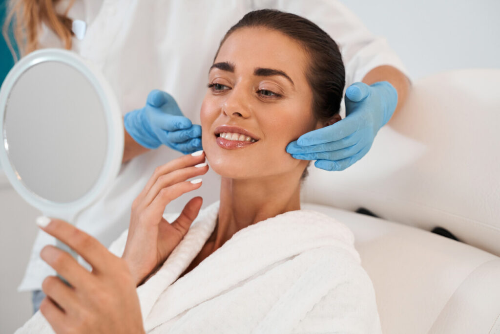 Female looking in mirror after cosmetic procedure. | Children's Skin ...